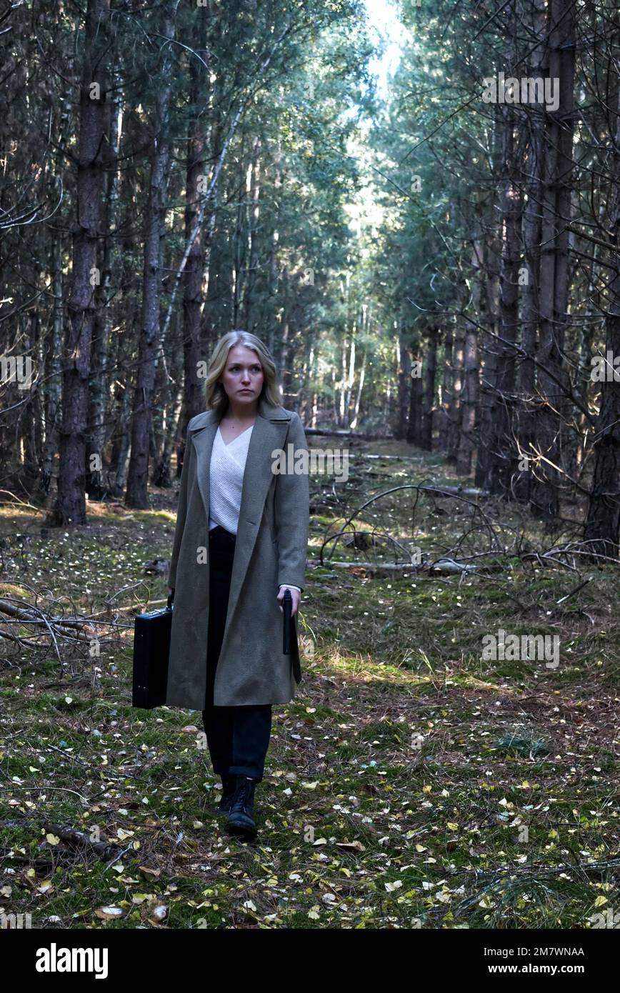 A young blonde women in long green coat walking down a path between ...
