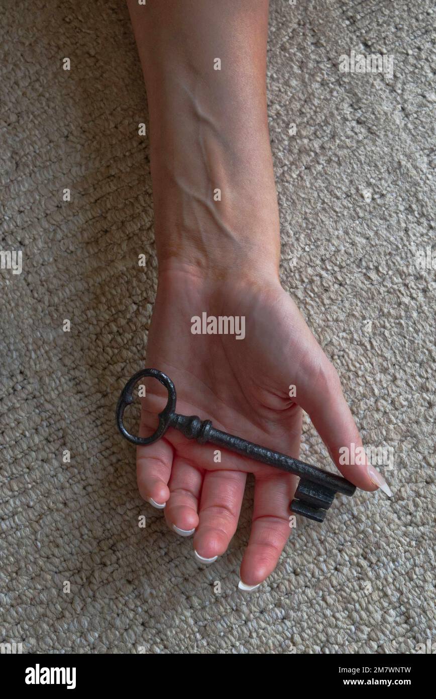 close up of young woman's hand holding an old key, laying on a carpet ...