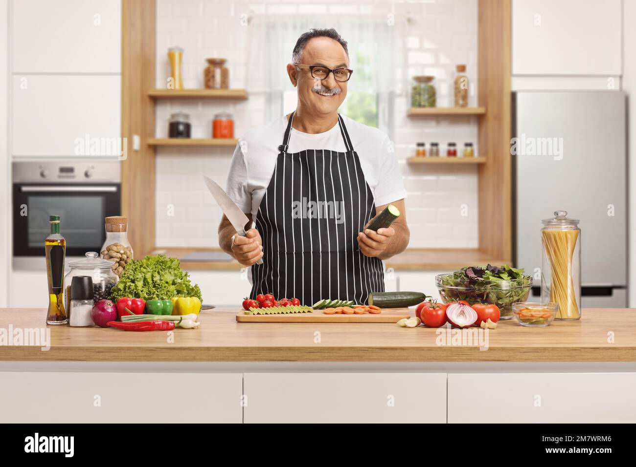 Mature man with an apron cutting a cucumber inside a kitchen Stock ...