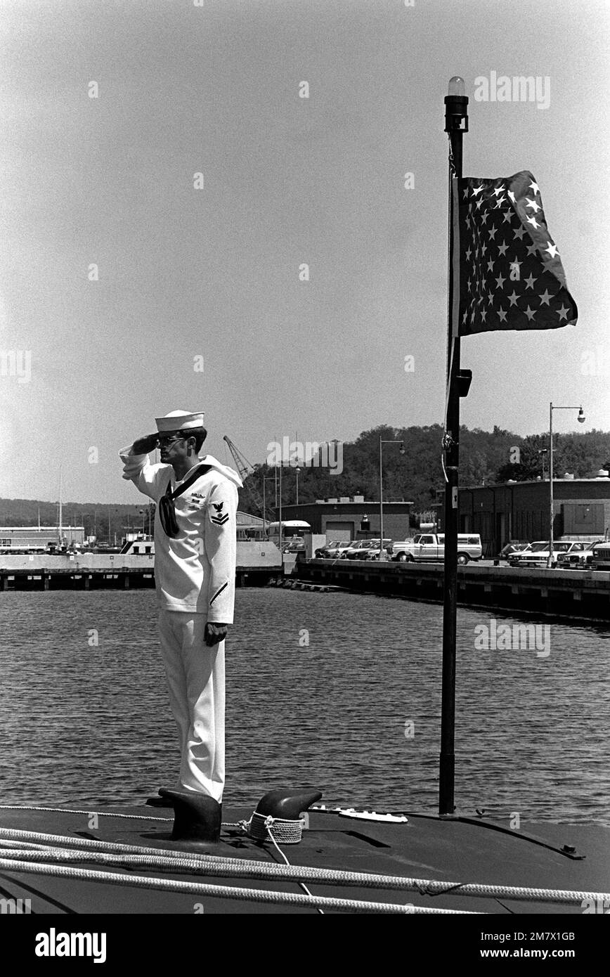 A crewman salutes after raising the colors at the conclusion of the ...