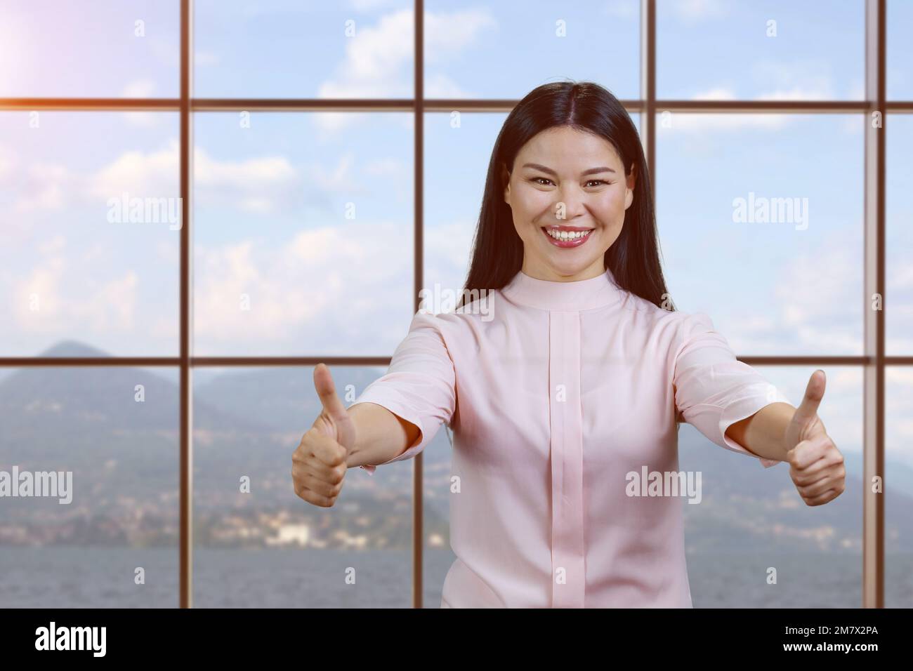 Portrait of young smiling asian woman giving two thumbs up. Checkered ...