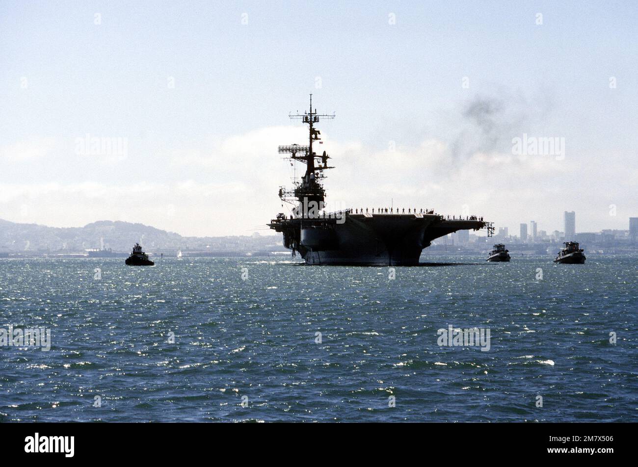 Crewmen line the rail as tug boats escort the aircraft carrier USS ...