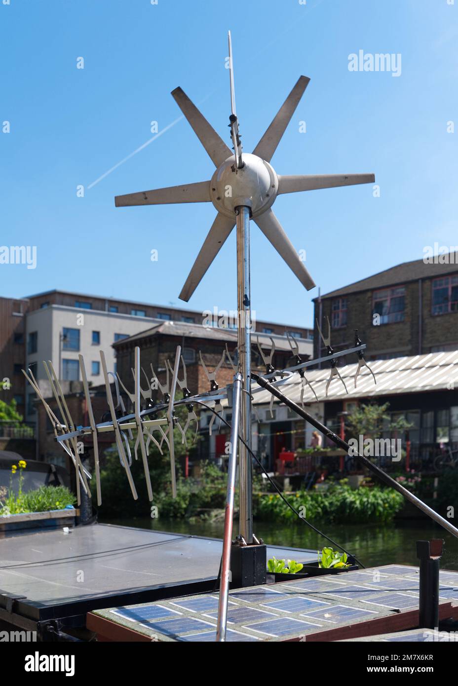 Wind turbine and solar panels atop a narrow boat moored on a canal ...