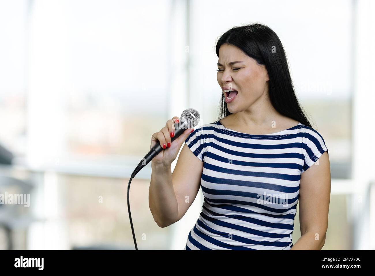 Young brunette asian woman is singing a song with microphone. Blurred ...