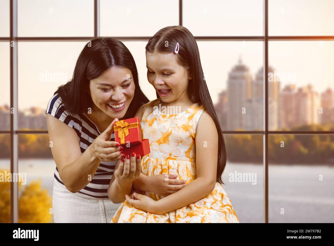 Young mother is opening a gift box for her surprised little daughter ...