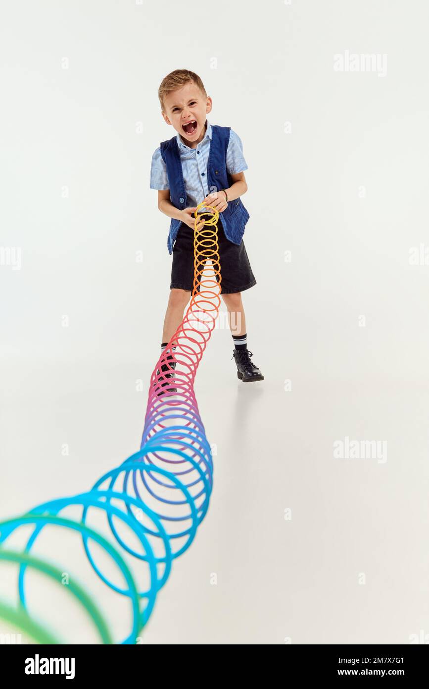 Boy, child in classical retro clothes playing with slinky toy over grey ...