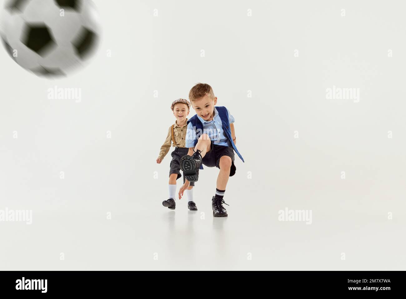 Boys, children in classical retro clothes playing football over grey ...