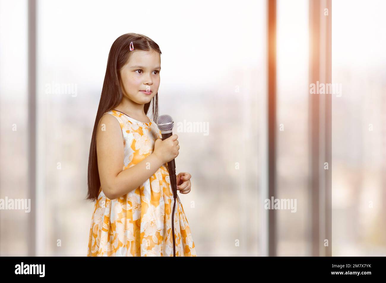 Cute little girl in dress is holding a microphone. Blurred indoor windows background Stock Photo ...