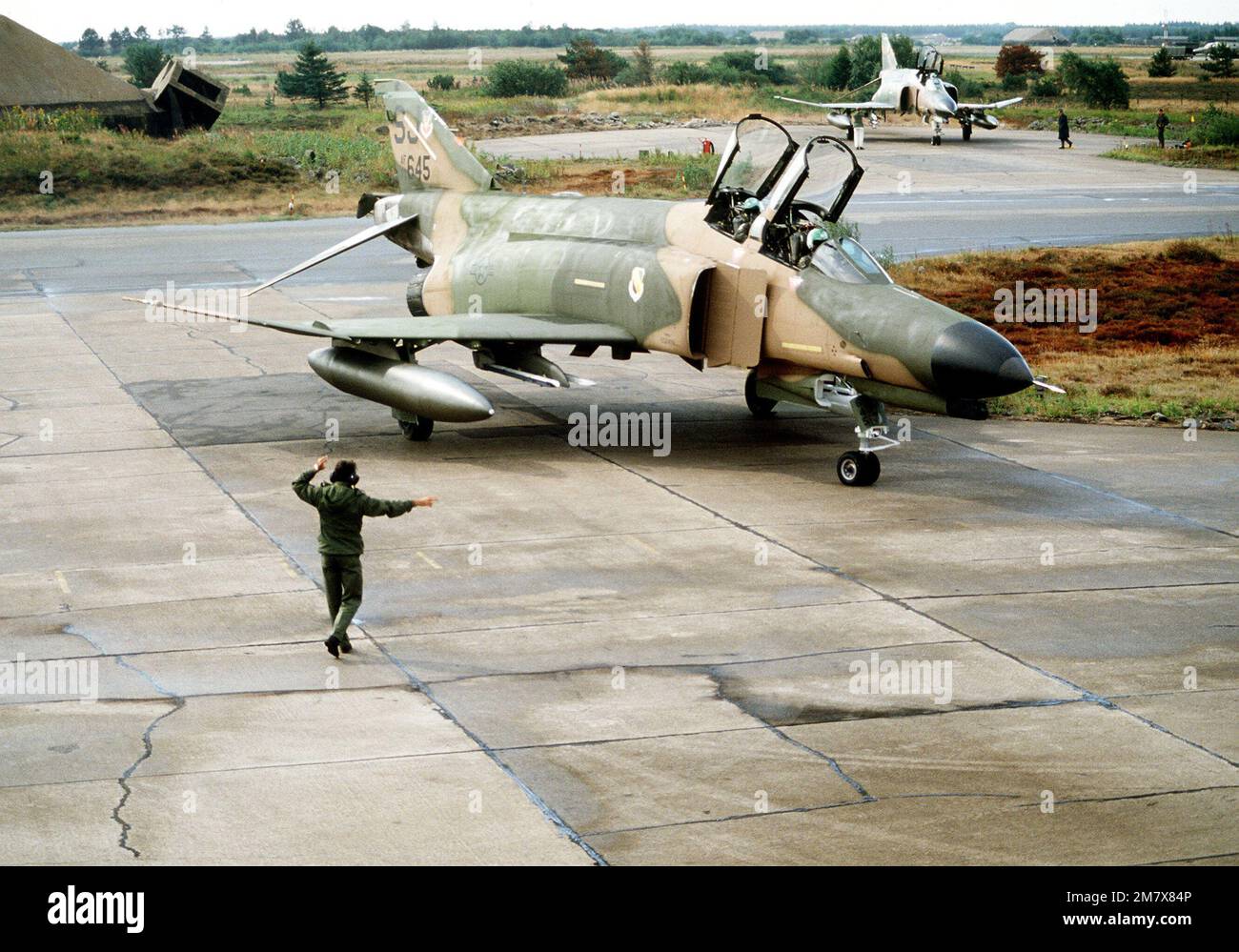 A ground crewman guides an F-4E Phantom II aircraft off the runway ...