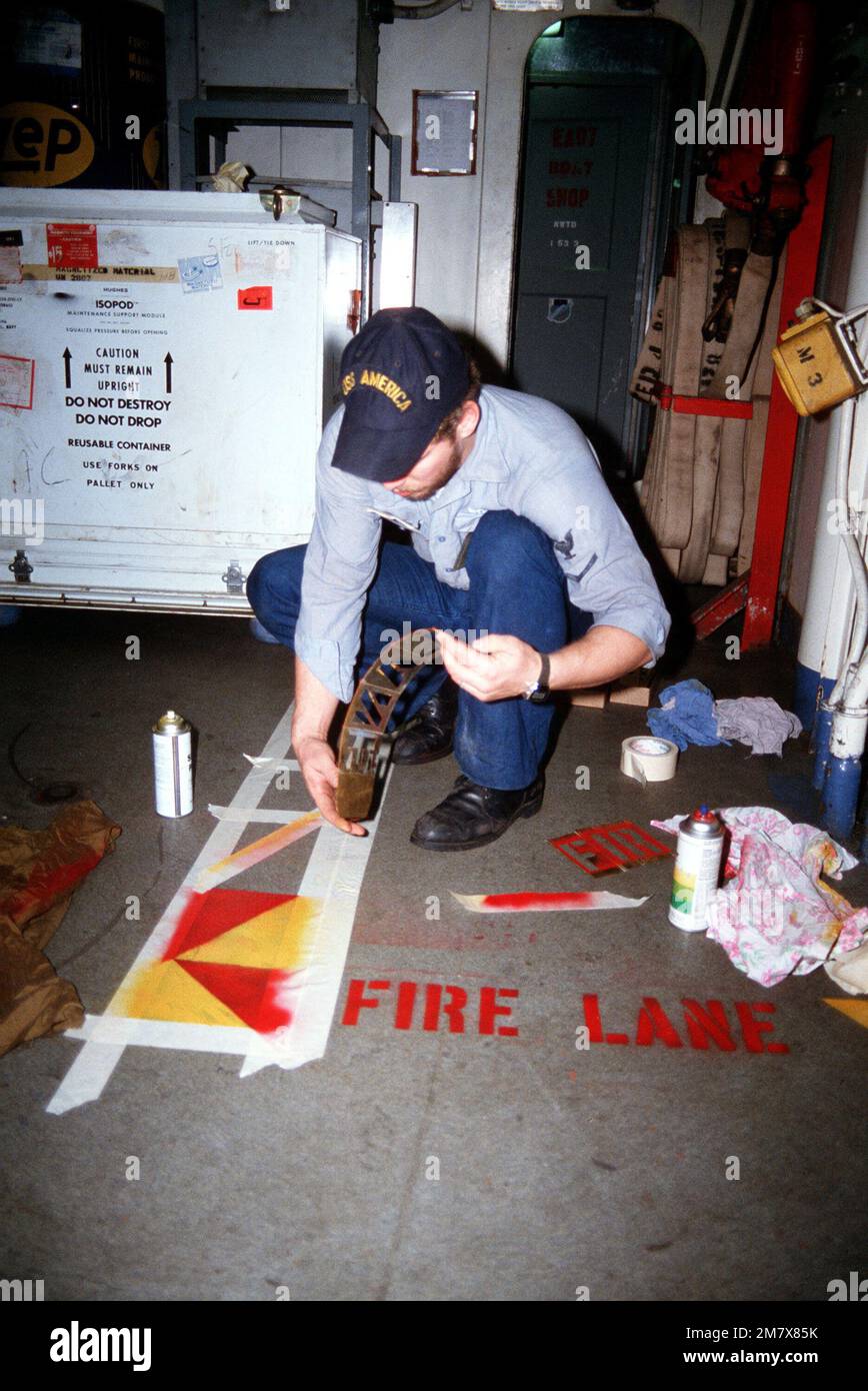 A crewman paints markings for a fire lane on the deck of the aircraft ...