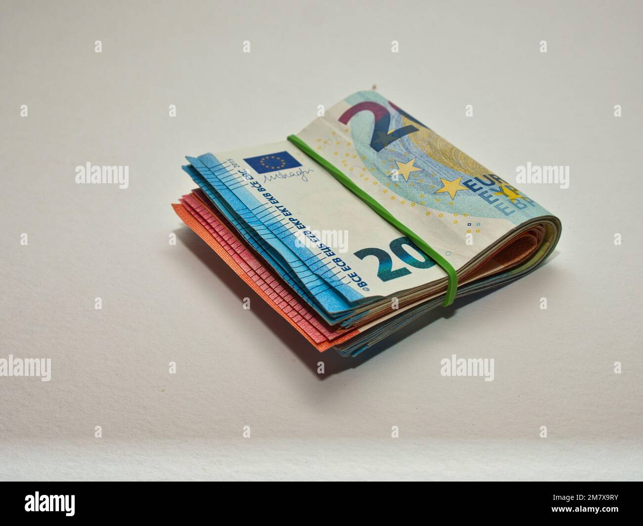 A wad of euro bills held tightly together by a rubber band on a white ...