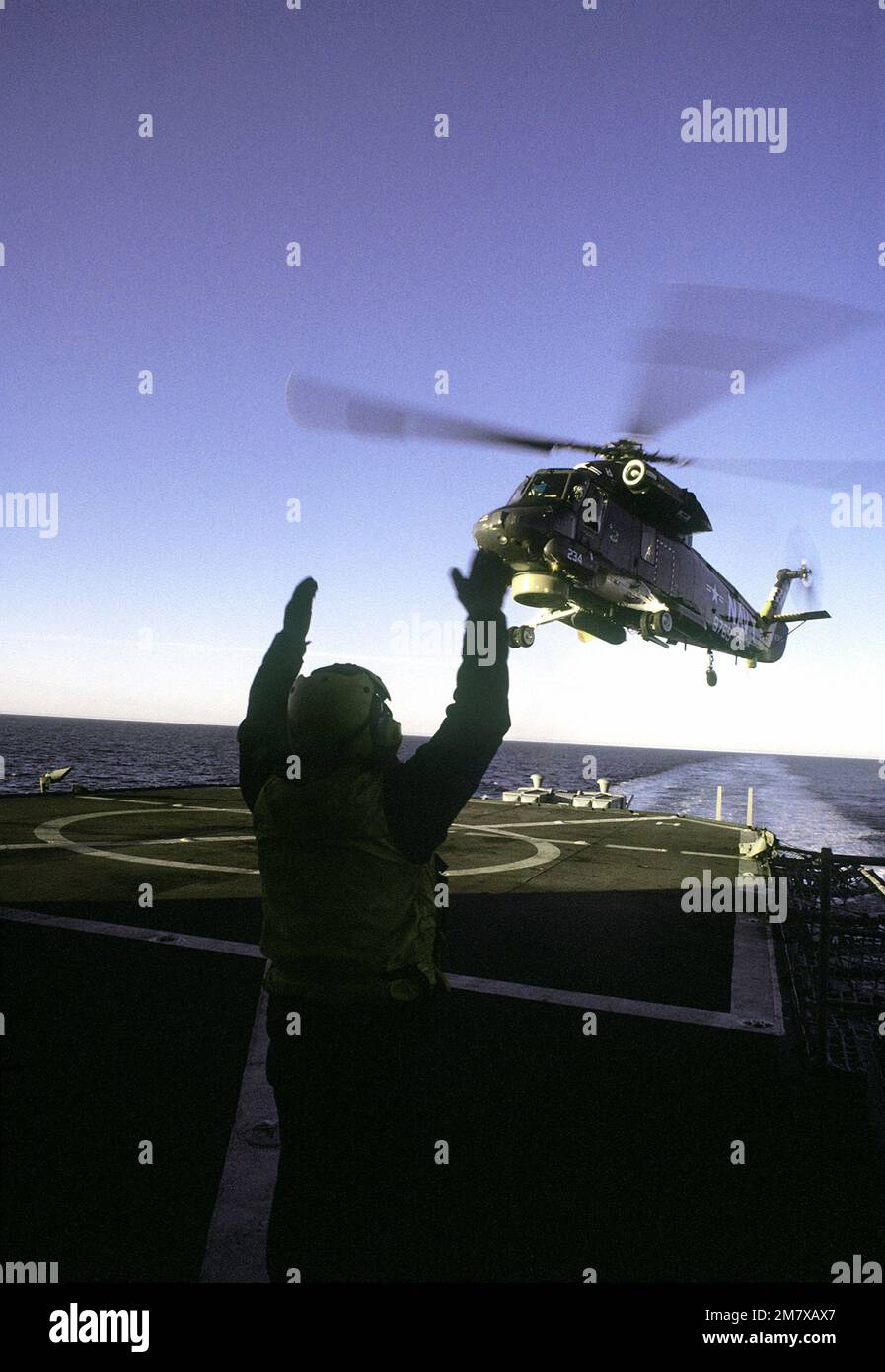 A flight deck crewman signals as SH-2F Seasprite light airborne multi ...