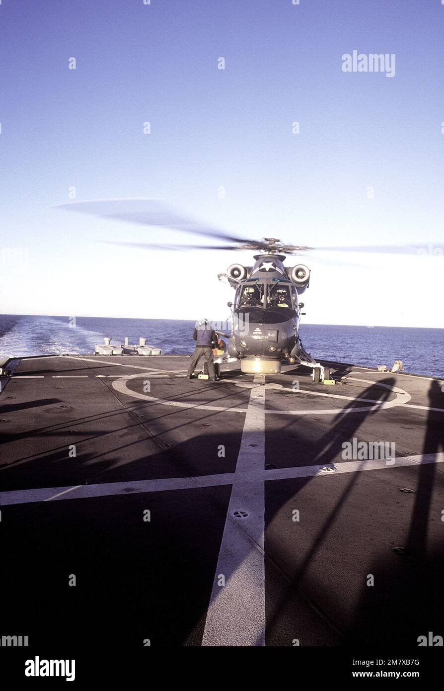 A flight deck crewman places chocks under the wheels of an SH-2F ...