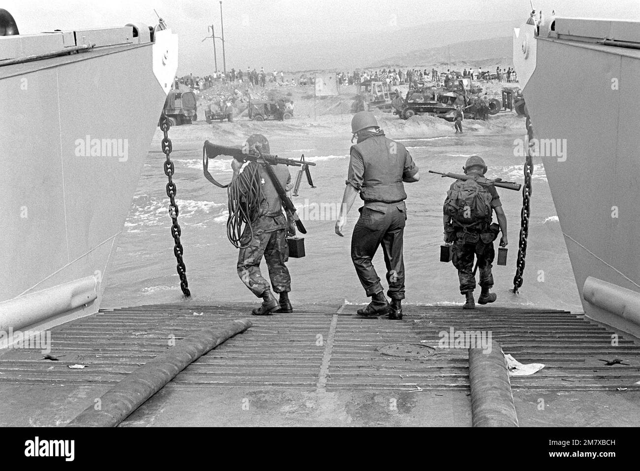 U.S. Marines carrying weapons and ammunition walk off the bow ramp of a ...
