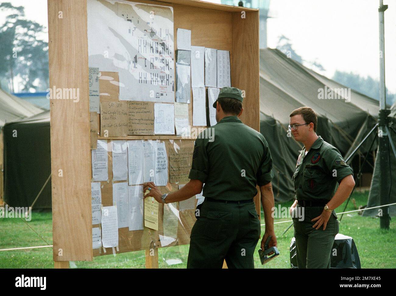 Two enlisted men read the bulletin board at the tent city area during ...