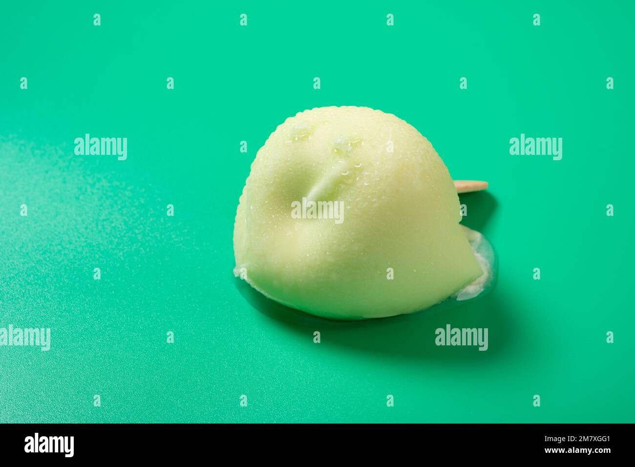 green apple shape and flavor popsice starts melting on green background ...