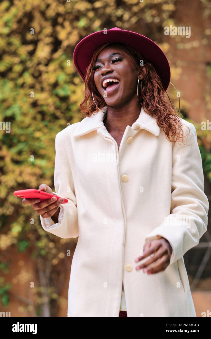 Stylish woman laughing while using mobile phone standing outdoors Stock Photo - Alamy