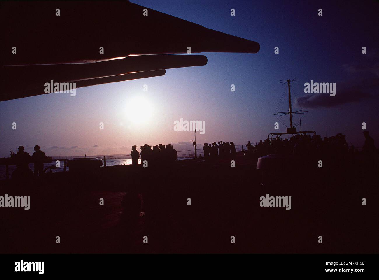 Crewmen and the ship's 16-inch/50-caliber gun barrels are silhouetted ...