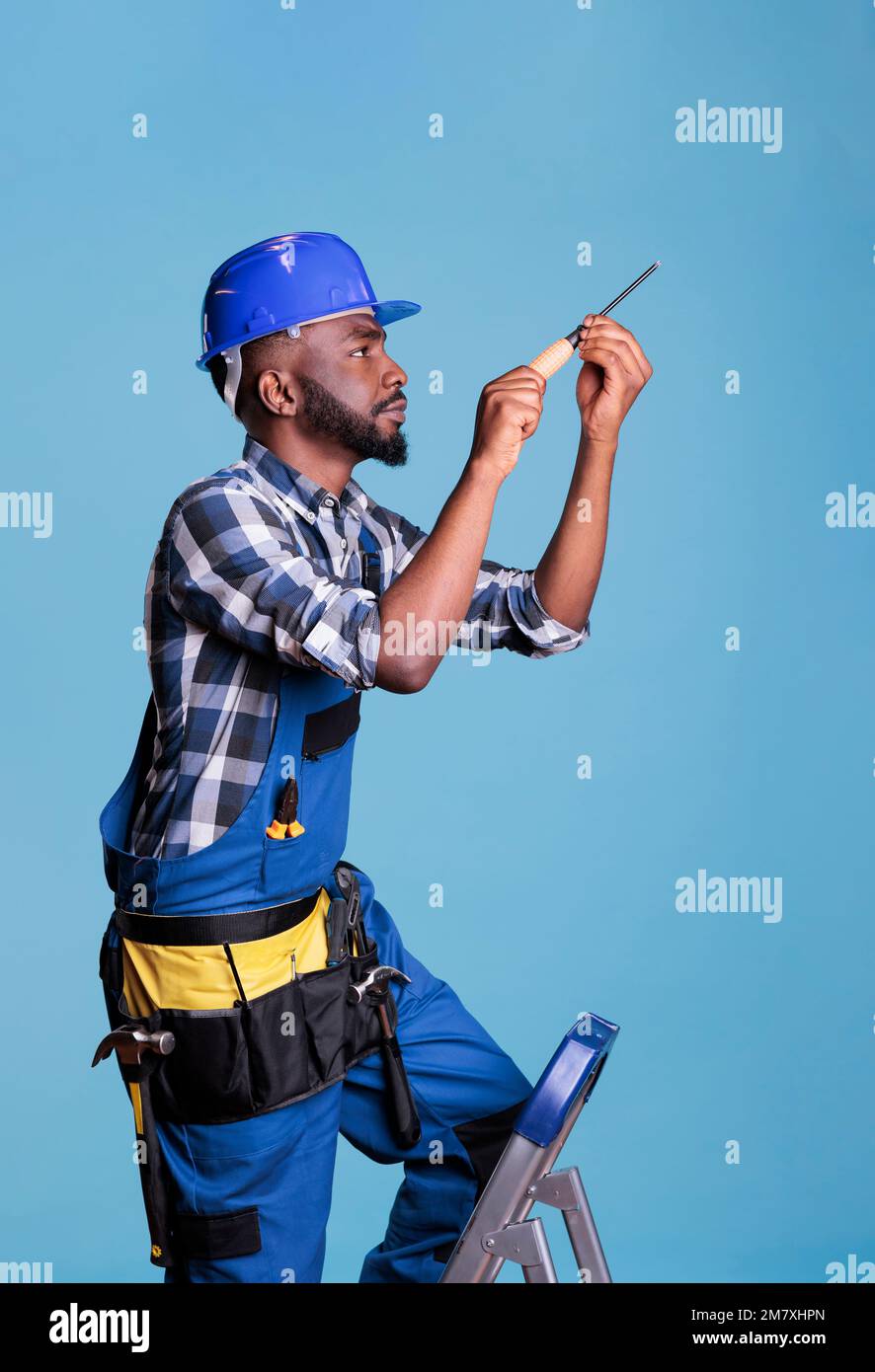 African American construction worker on ladder repairing something with ...