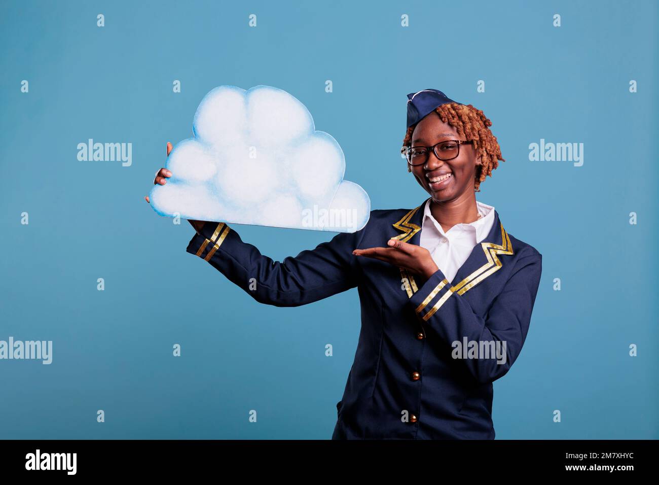 Female flight attendant smiling while holding paper cloud against blue ...