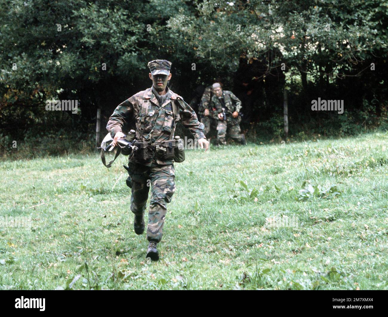 Camouflaged security police, armed with M-16 rifles, enter a clearing ...