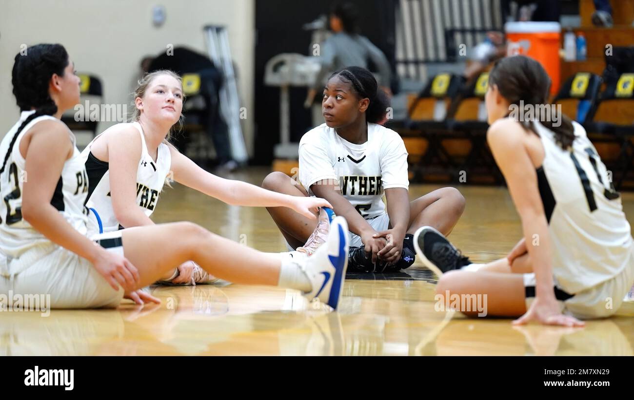A young female team stretching on an indoor court at a girls fall high school basketball game ...