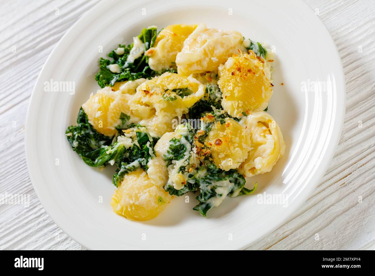 portion of cheesy baked shell pasta with green leafy kale topped with ...