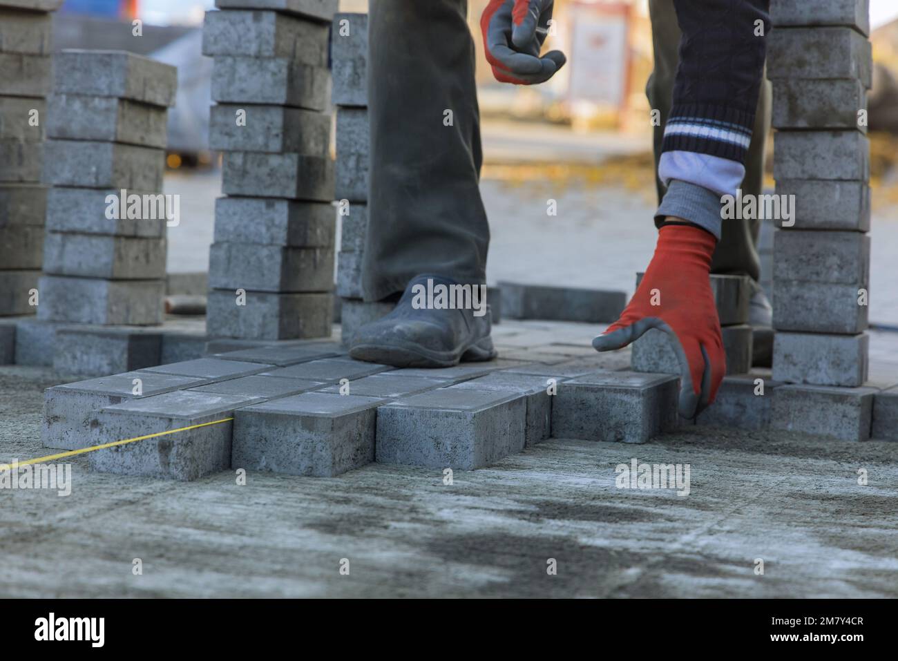 Master who is laying gray concrete paving brick slabs on sand foundation bases in courtyard of ...