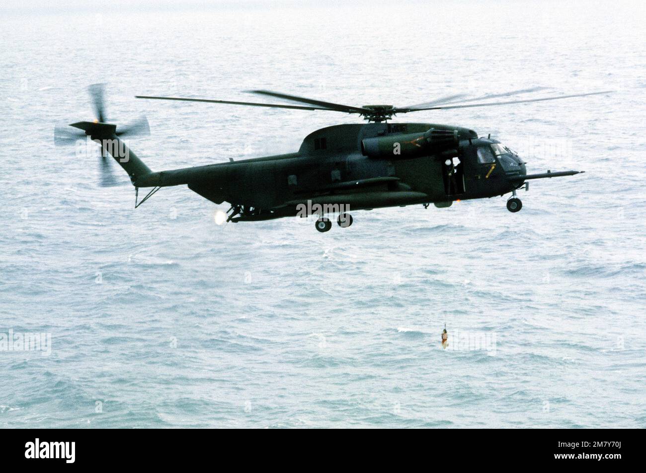 A right side view of an HH-53 Super Jolly helicopter reeling down a ...
