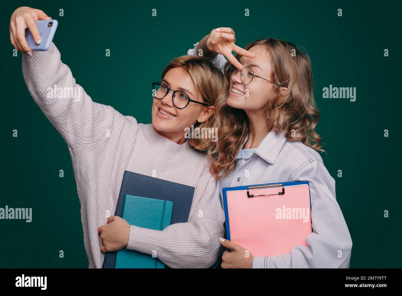 Portrait of two happy young girls holding copybooks and taking a selfie ...