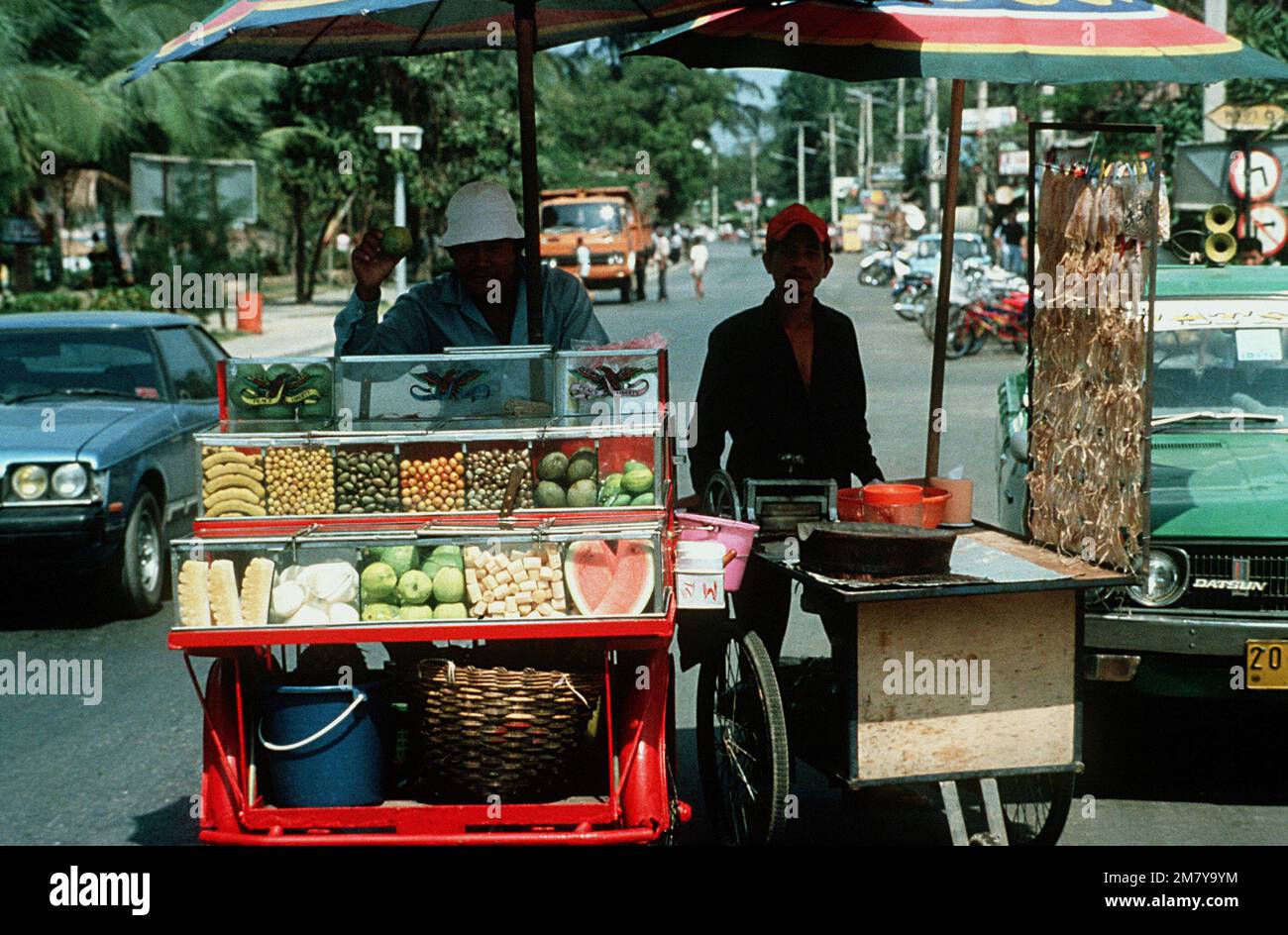 Vendors sell fruit and Thai food from their carts on a busy street ...