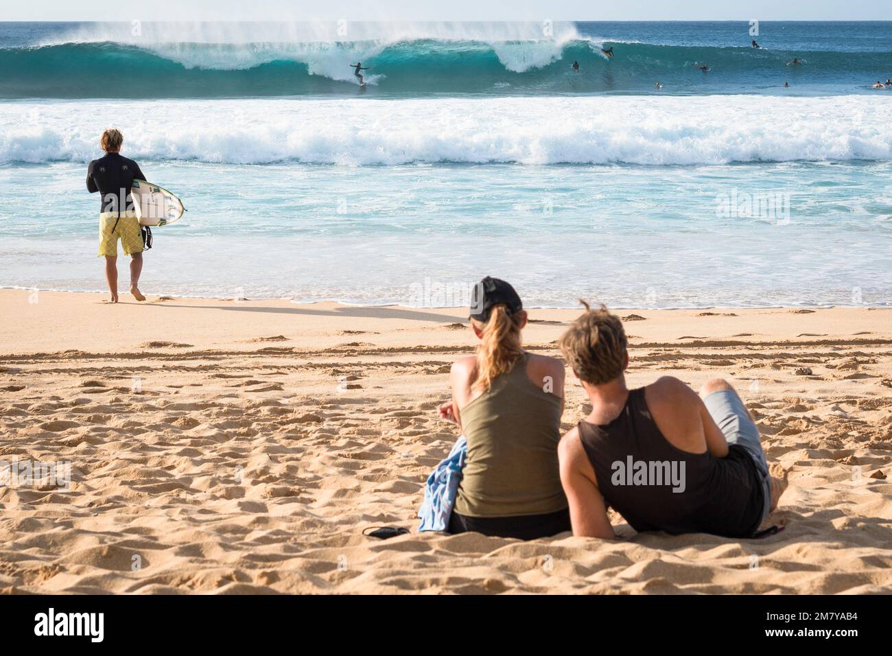 Young surfer and a couple are watching big wave surfing Stock Photo - Alamy