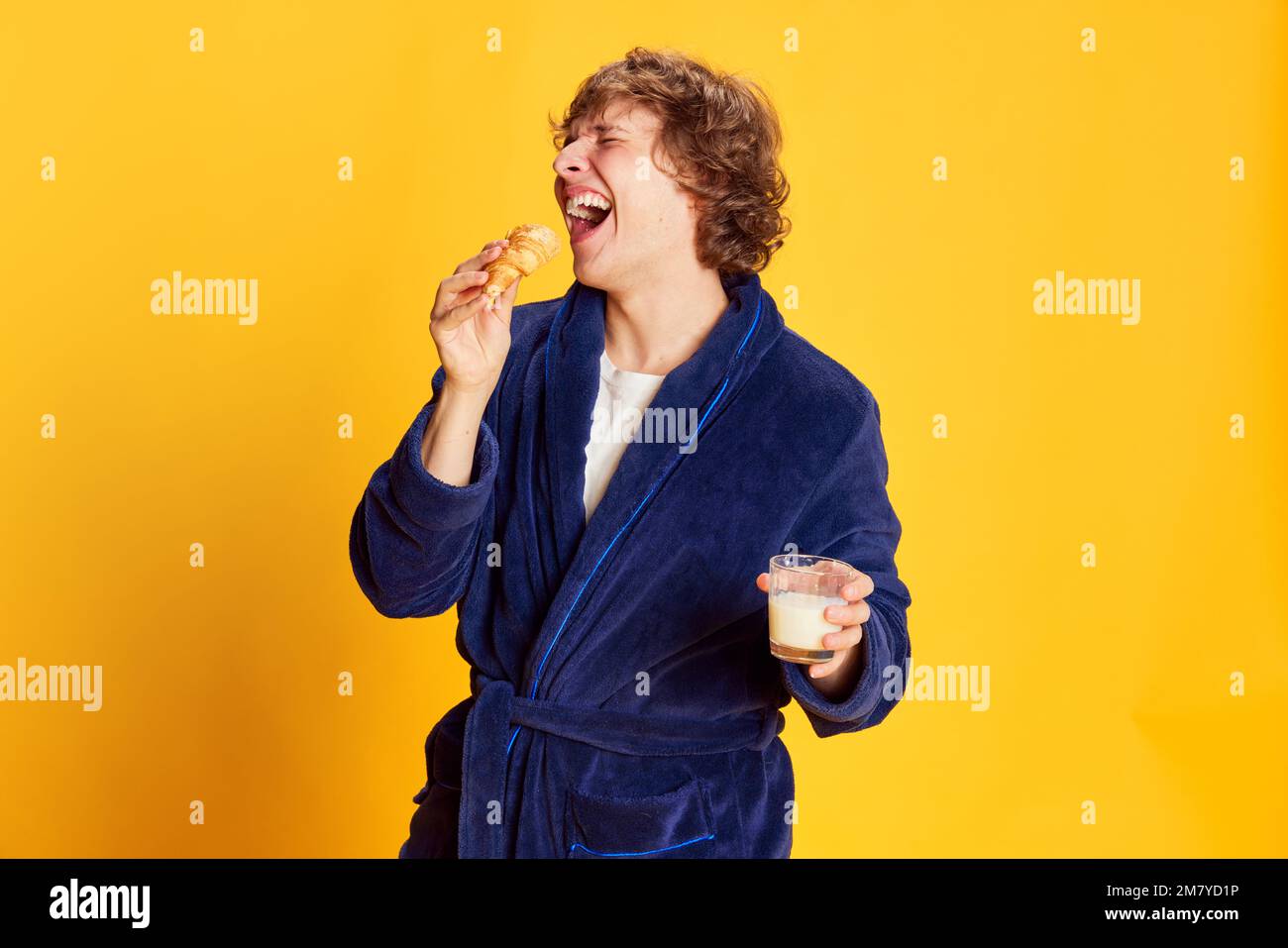 Laughing young man wearing bathrobe and having breakfast isolated over ...