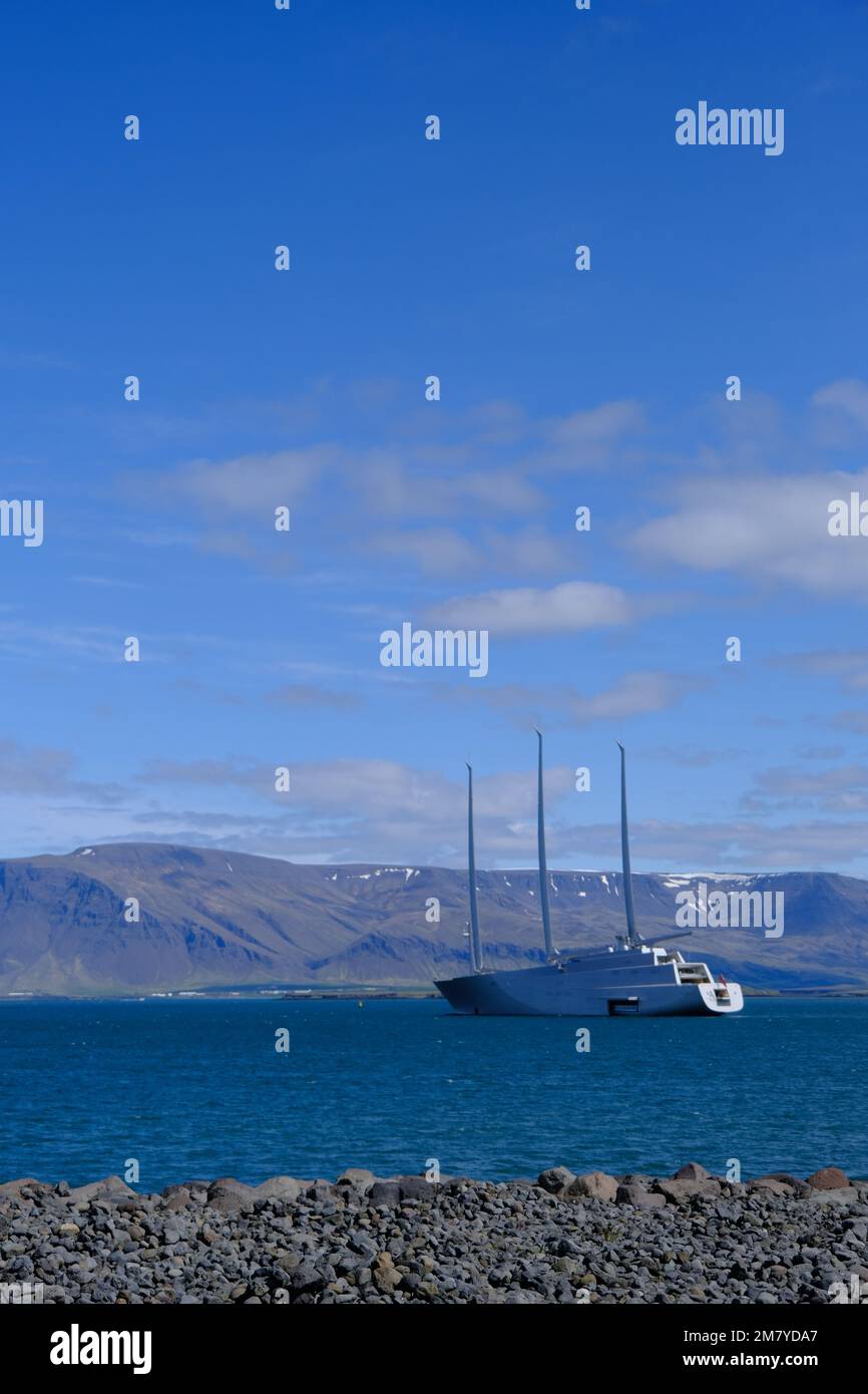 A vertical shot of a sailing yacht on the blue sea before the mountains ...