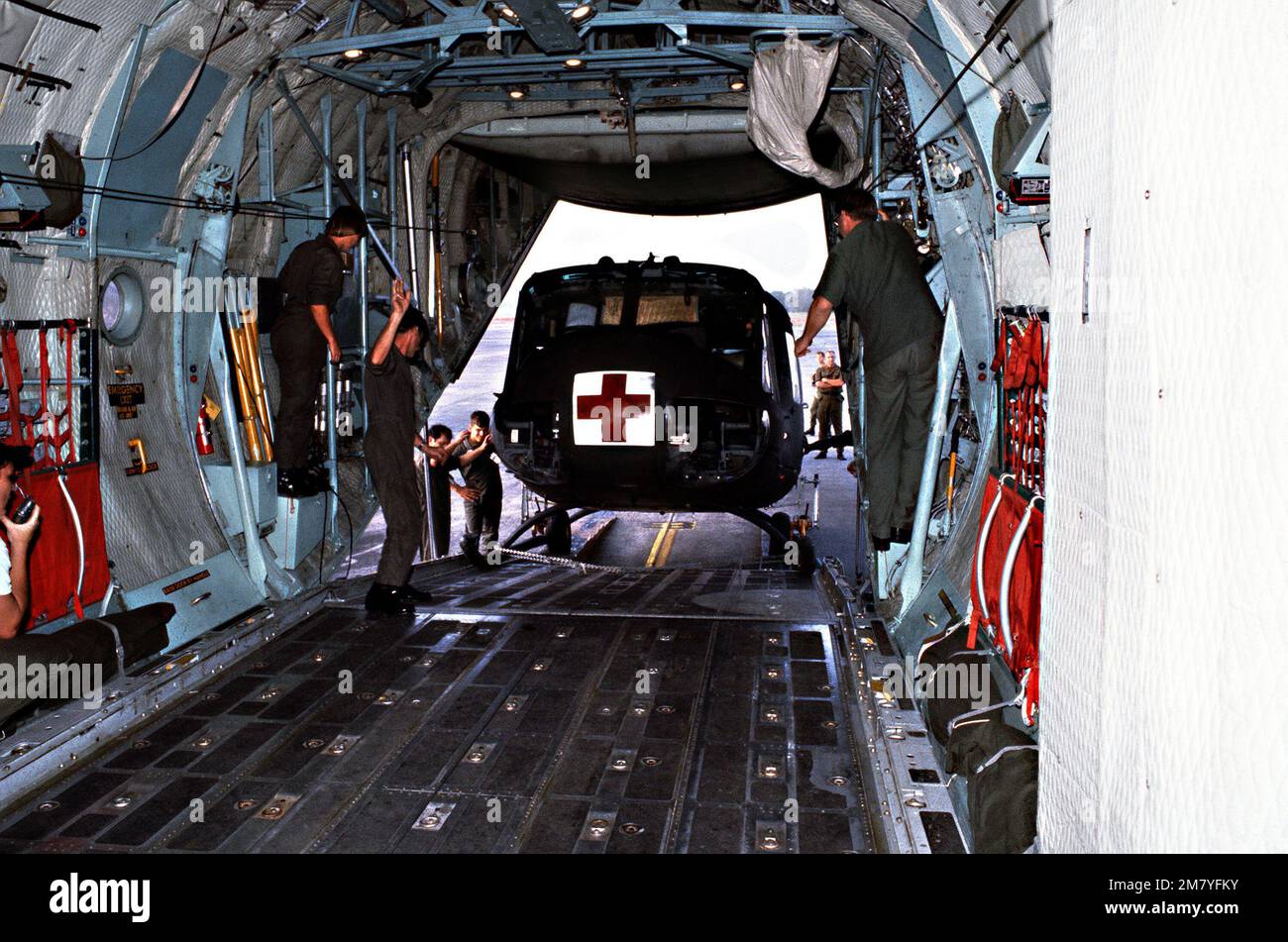 A UH-1 Iroquois helicopter is guided into the cargo hold of a C-130 ...
