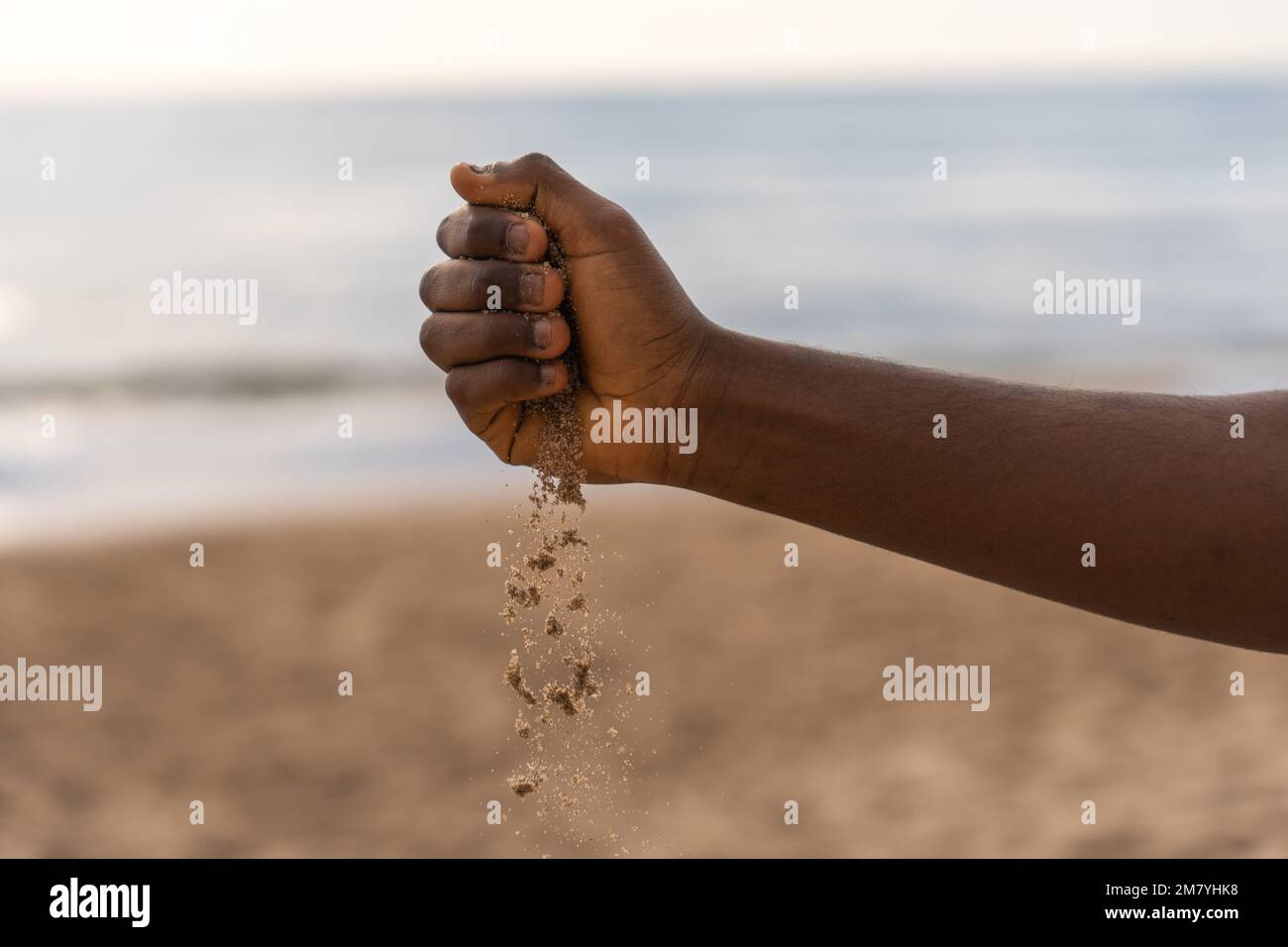 Crop anonymous African American male pouring sand from hand during day ...