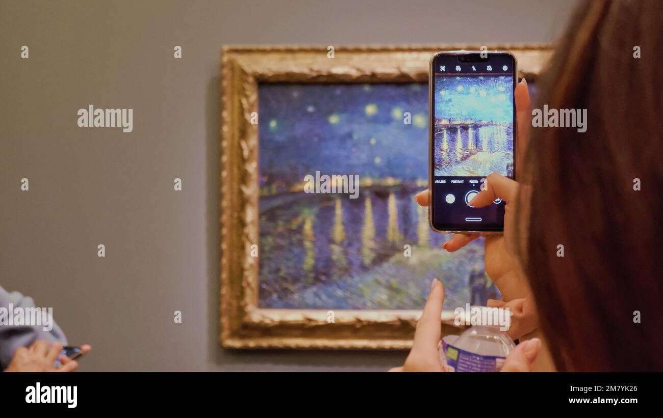 A female taking a picture of a painting with her cell phone in an art ...