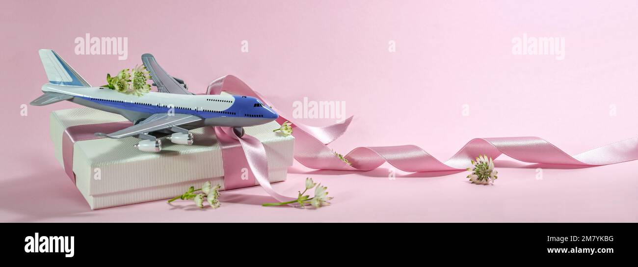 Gift box with a toy airplane, long ribbon and some flowers on a light ...