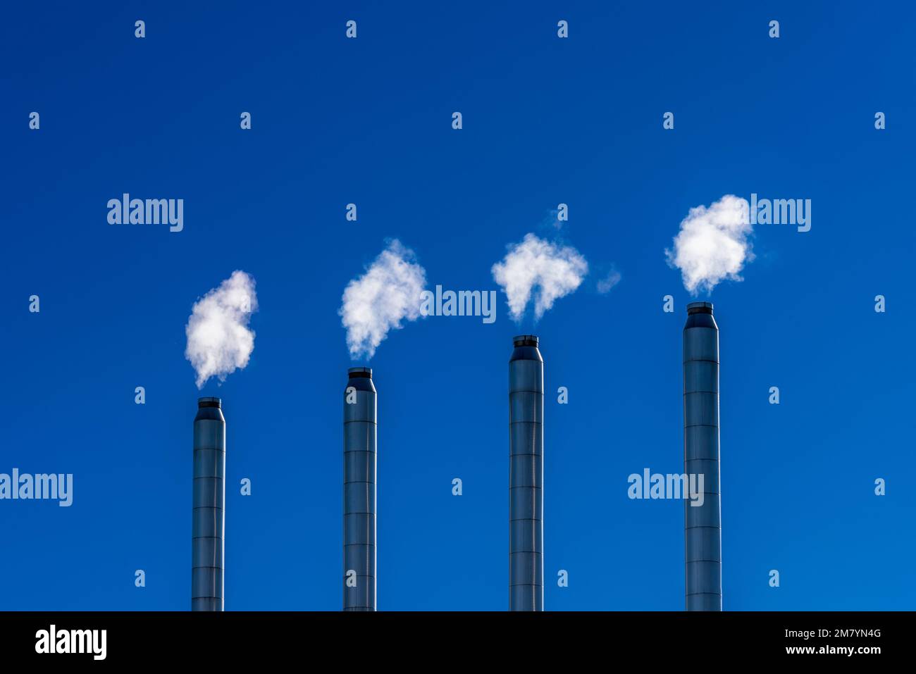 Four steel chimneys with white smoke over clear blue sky; energy and ...