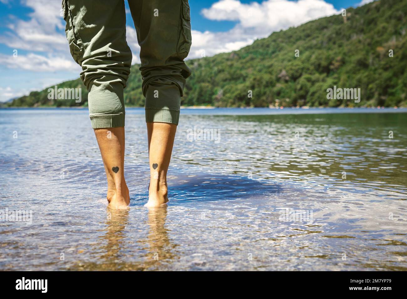 Woman on the shore of the lake walking with her feet in the cold water ...