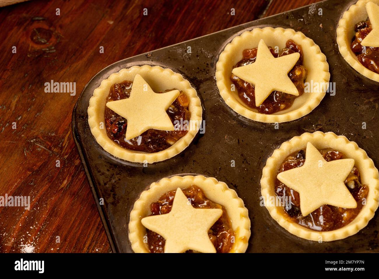 Closeup of star topped mince pies in a dark metal bun tin before baking ...