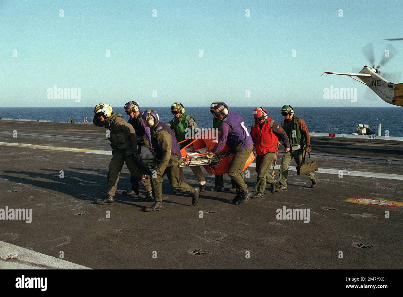 Crewmembers carry a litter across the flight deck of the aircraft ...