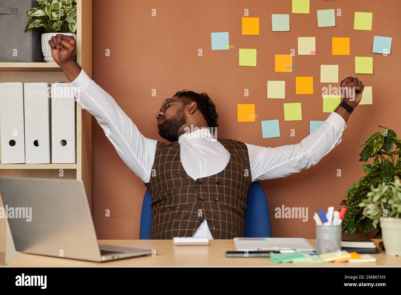 Indian entrepreneur sitting at office desk and stretching after ...