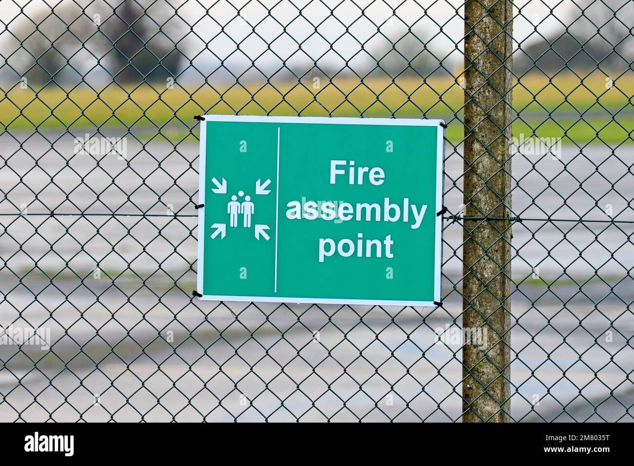Green and white Assembly Point sign fixed to a chain link fence Stock ...