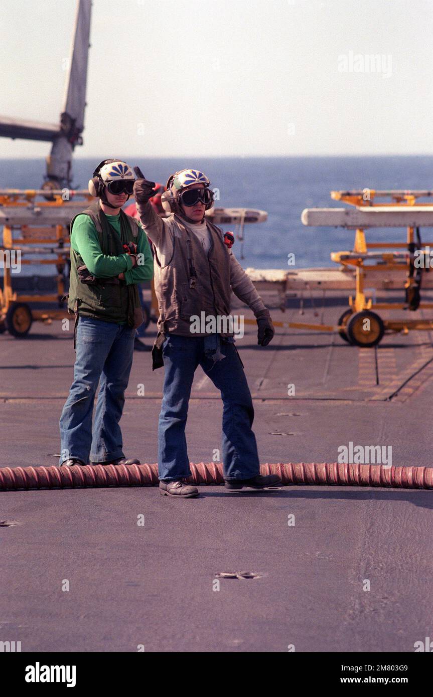 A flight deck crew member signals to a pilot during flight operations ...