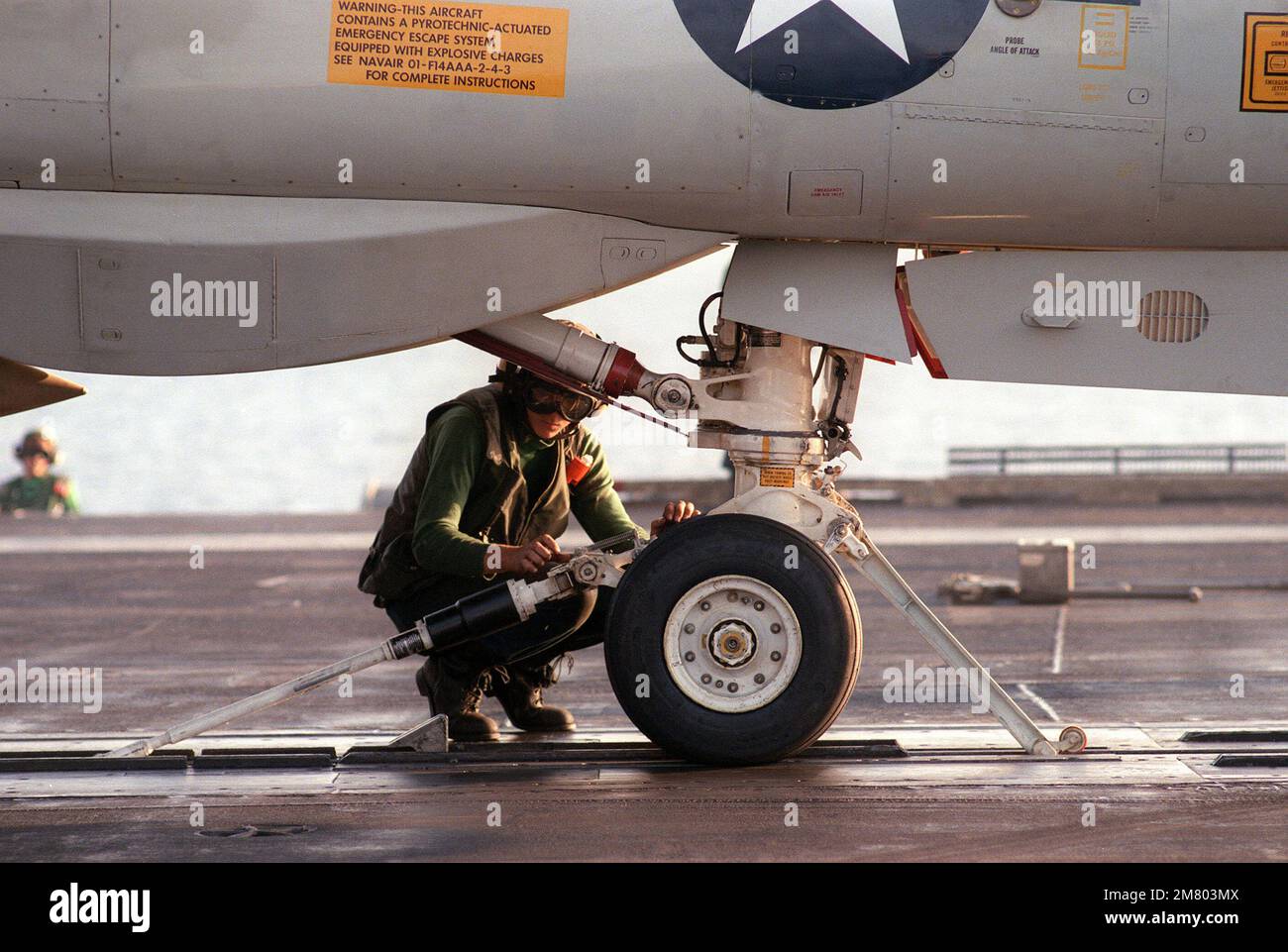 A flight deck crew member checks the shock absorbers attached to an F ...