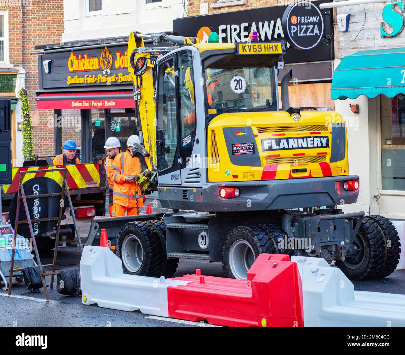 Digger operated by Flannery parked in London street and several workmen ...