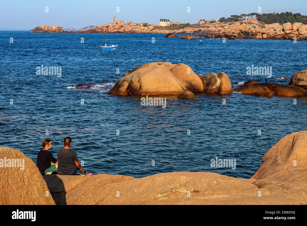 COUPLE WITH A VIEW FROM THE PINK GRANITE BOULDERS OF THE PLOUMANACH LIGHTHOUSE AT SUNSET, RENOTE ...