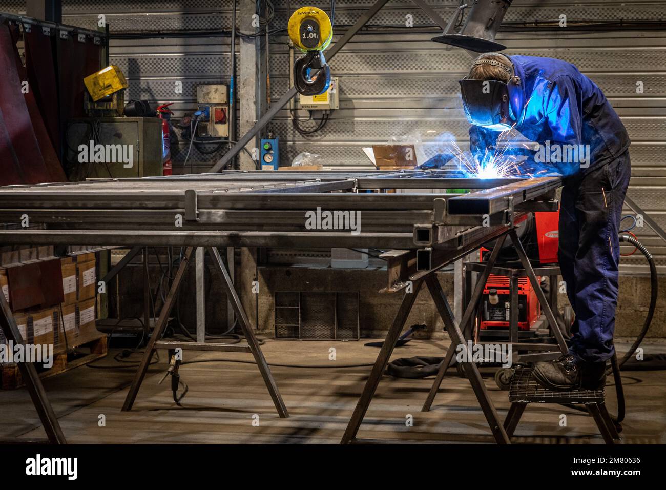 WELDING STATION, WELDER WORKING ON THE ASSEMBLY OF METAL PARTS IN HIS ...