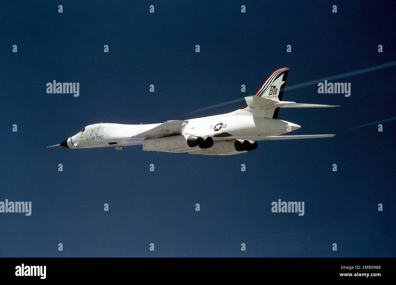 An air-to-air left rear view of a B-1B bomber aircraft with contrails ...